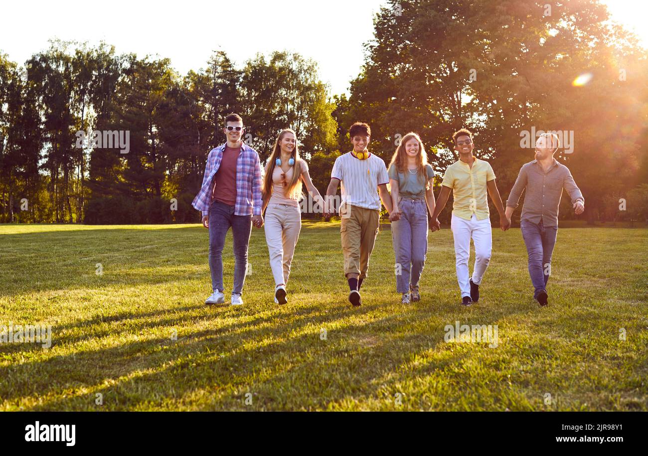 Cheerful positive multiracial friends holding hands walking on green ...