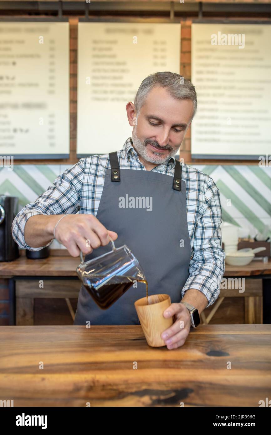 Barista pouring coffee to the coffee mug and looking contented Stock ...