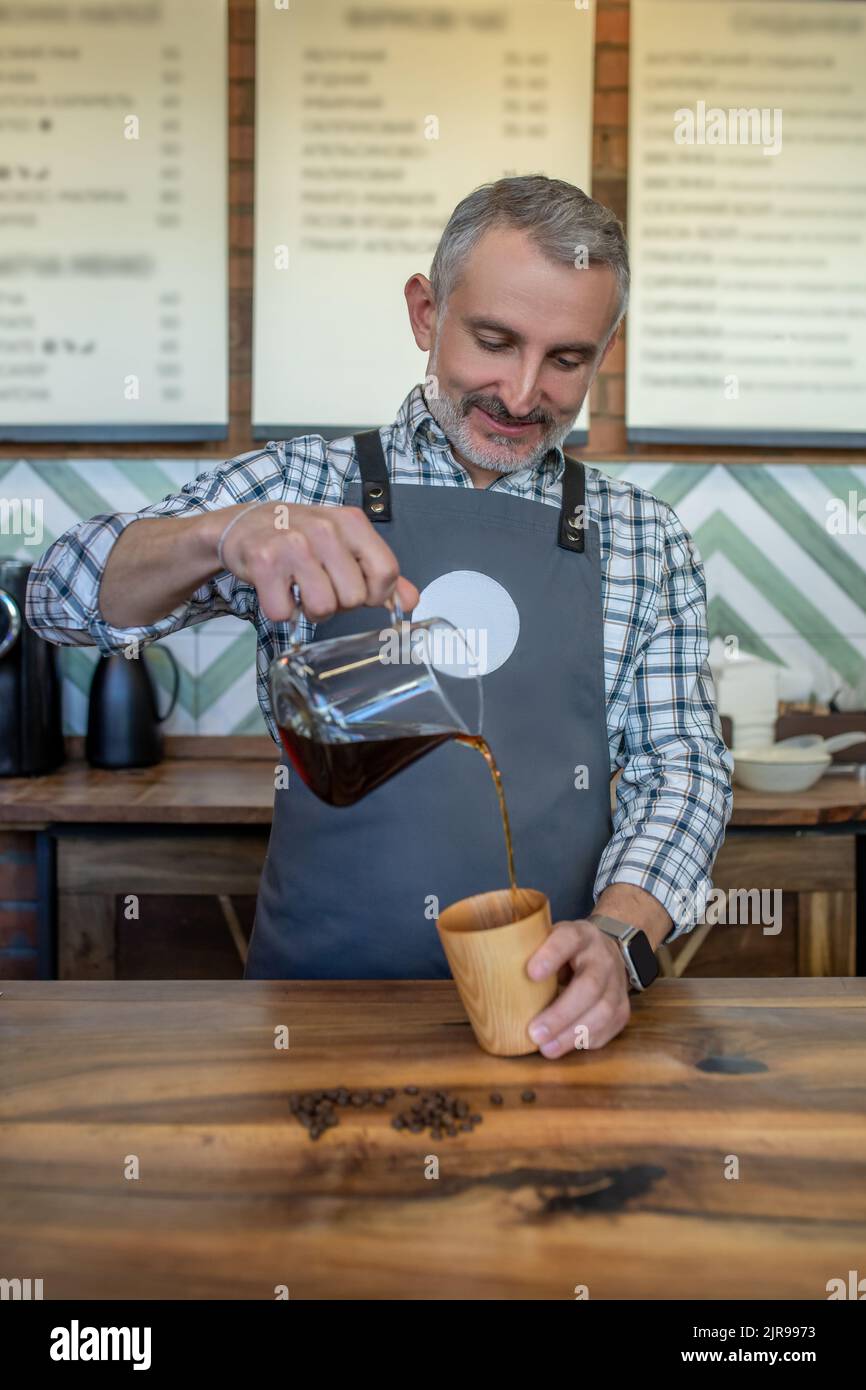 Barista pouring coffee to the coffee mug and looking contented Stock ...