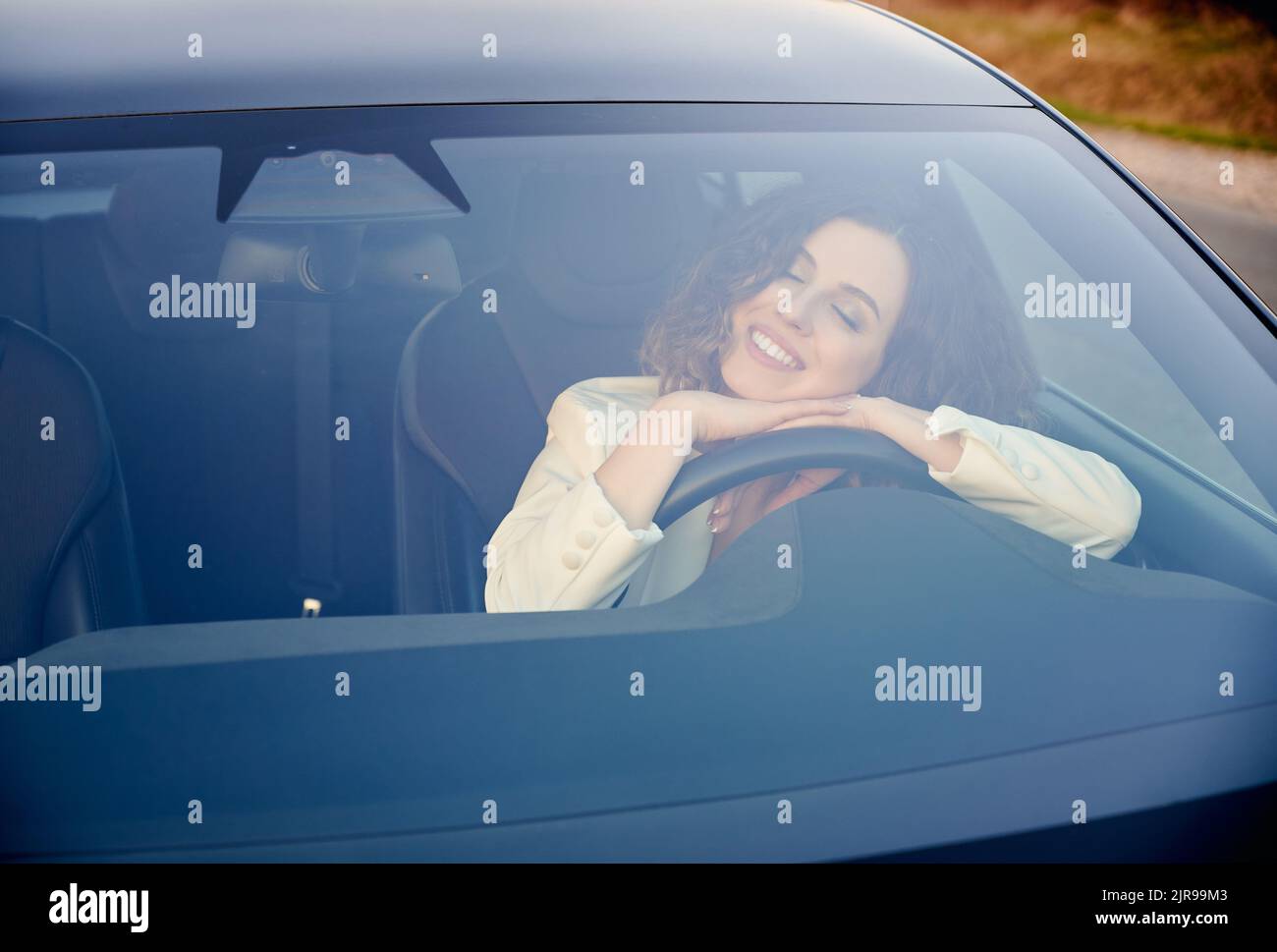 Young woman sitting behind glass in electric car with closed eyes ...