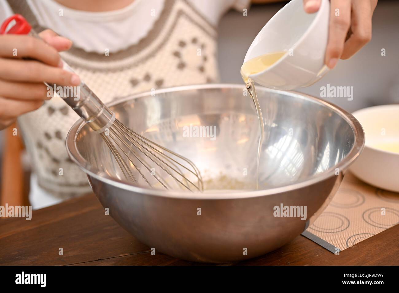 A female pouring a cup of egg white in the mixing bowl with the cupcake ...