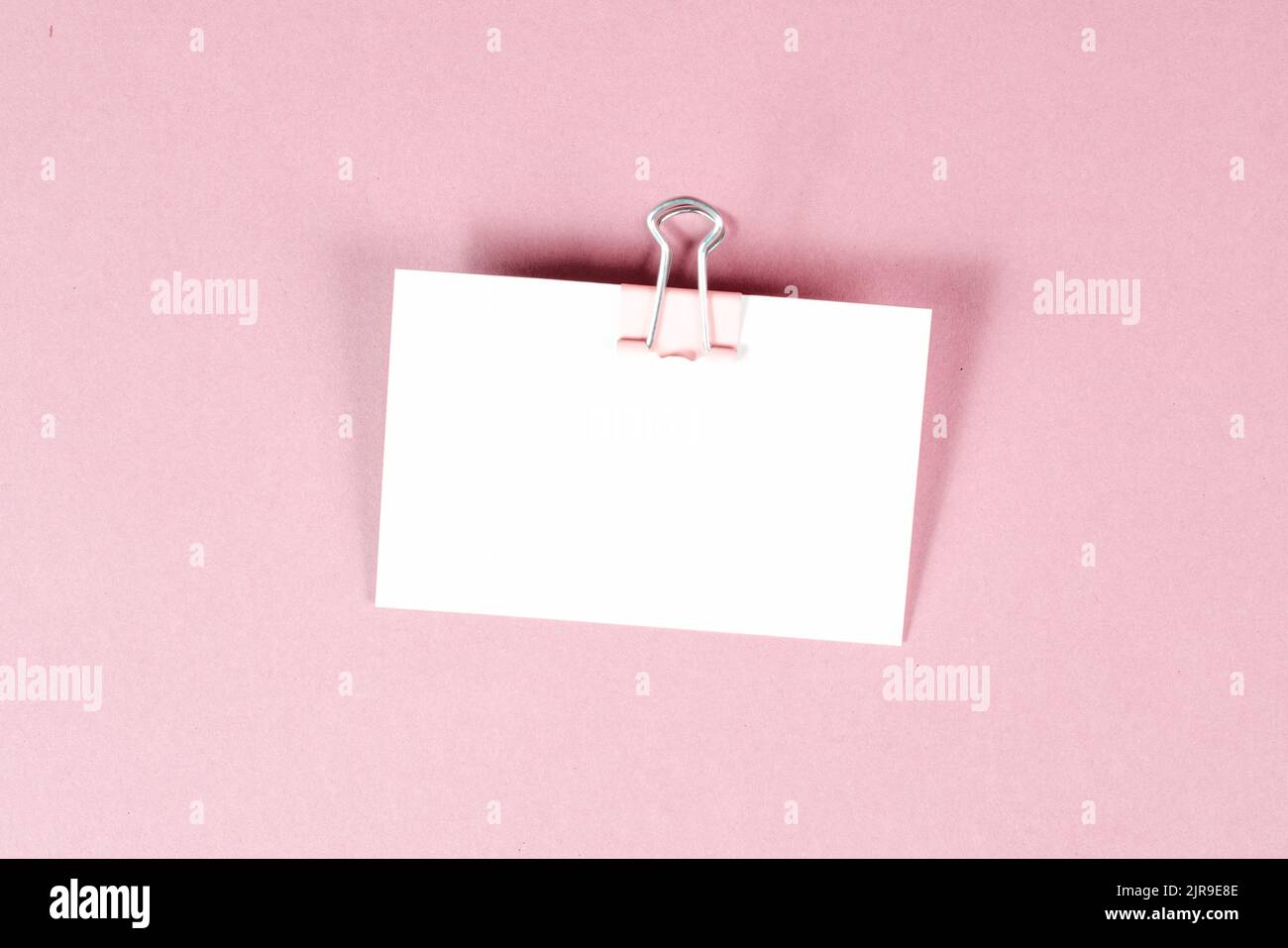 Blank white paper with a paperclip on a pink colored background, copy ...