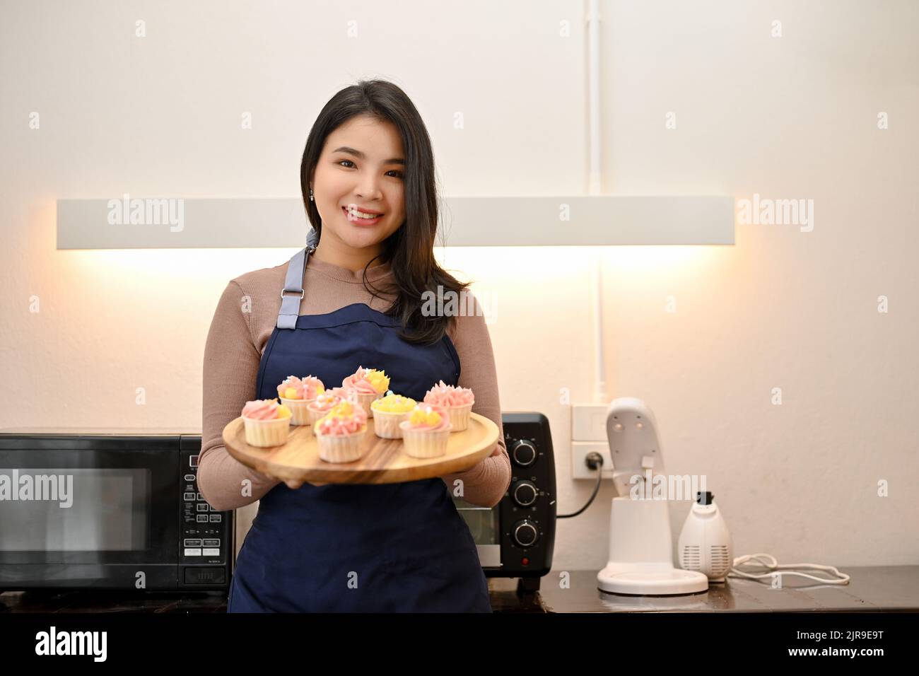 Portrait of young beautiful Asian woman making cupcake and showing ...