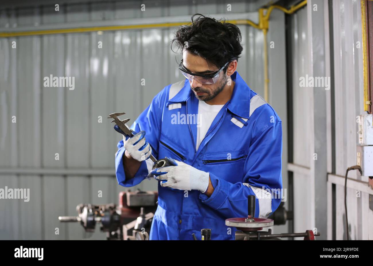 Male car operator wearing blue overalls,cap and gloves working under ...