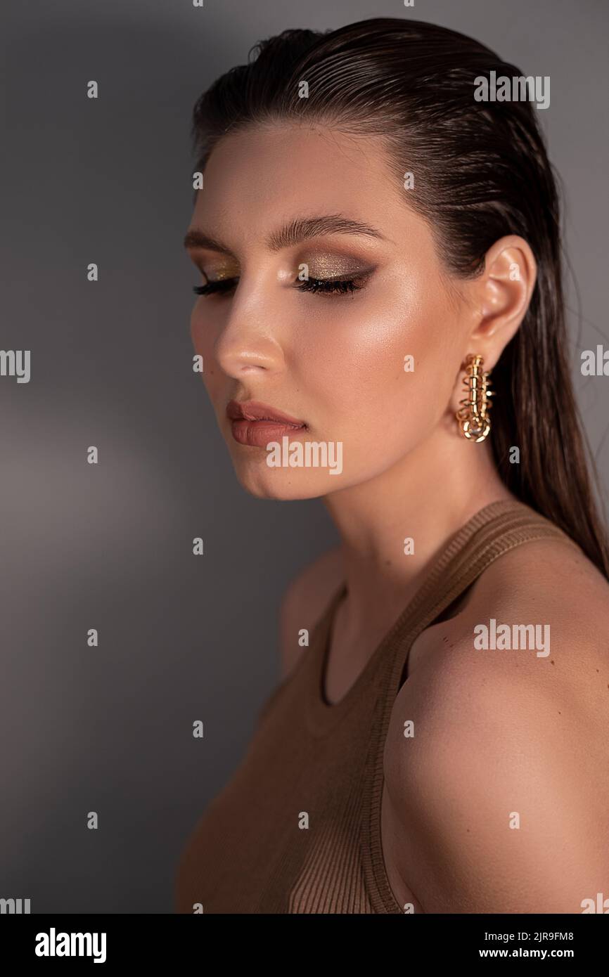 Side view of young wonderful woman with long dark hair, bright shining make-up, wear golden ...