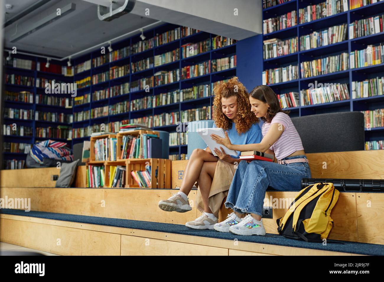 Vibrant full length portrait of two teenage girls reading books in ...