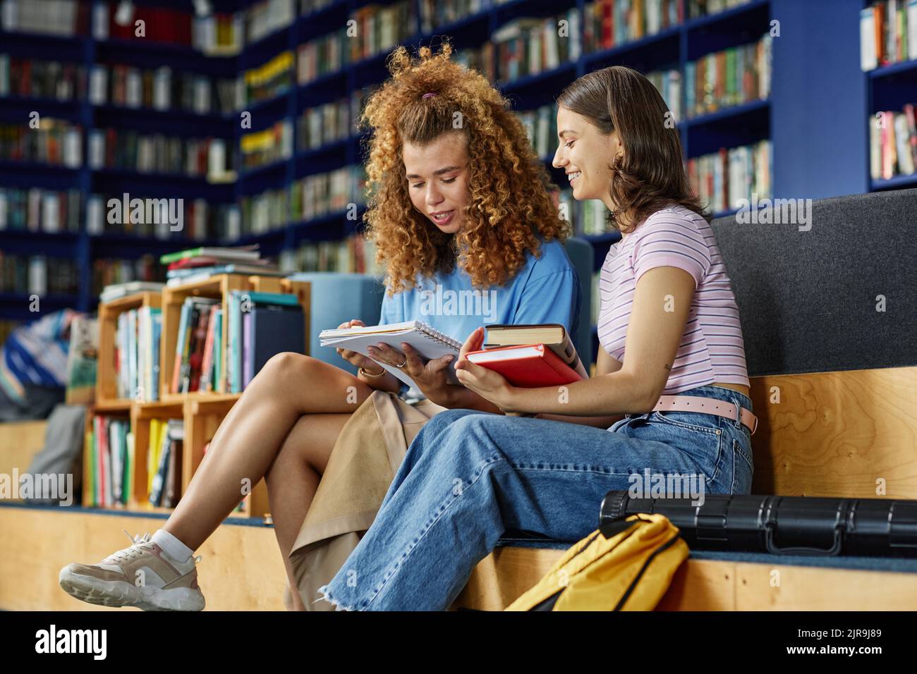 Vibrant portrait of two young girls reading books in college library ...