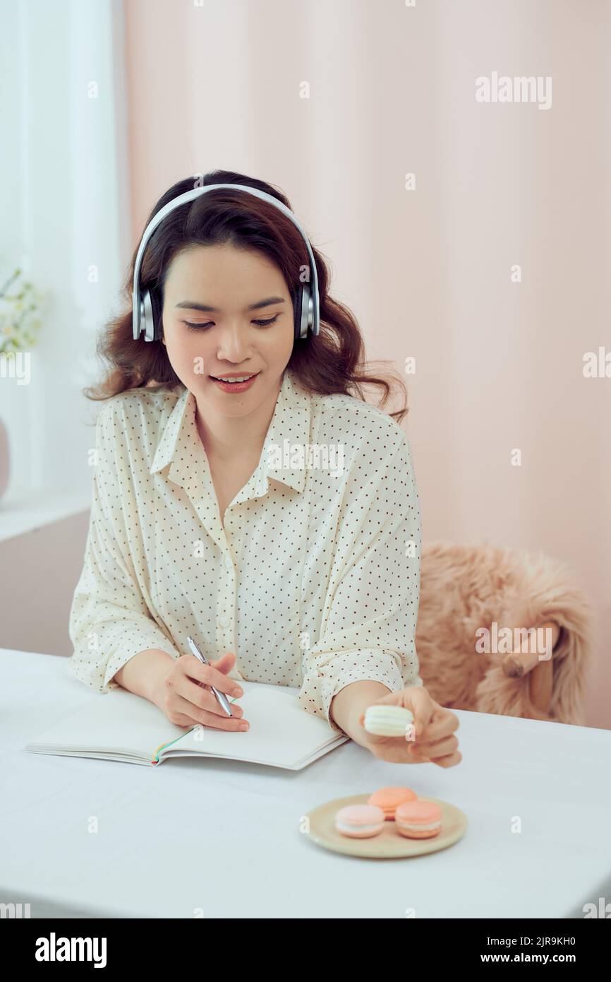 Asian young girl wearing headphones eating macarons and reading books ...