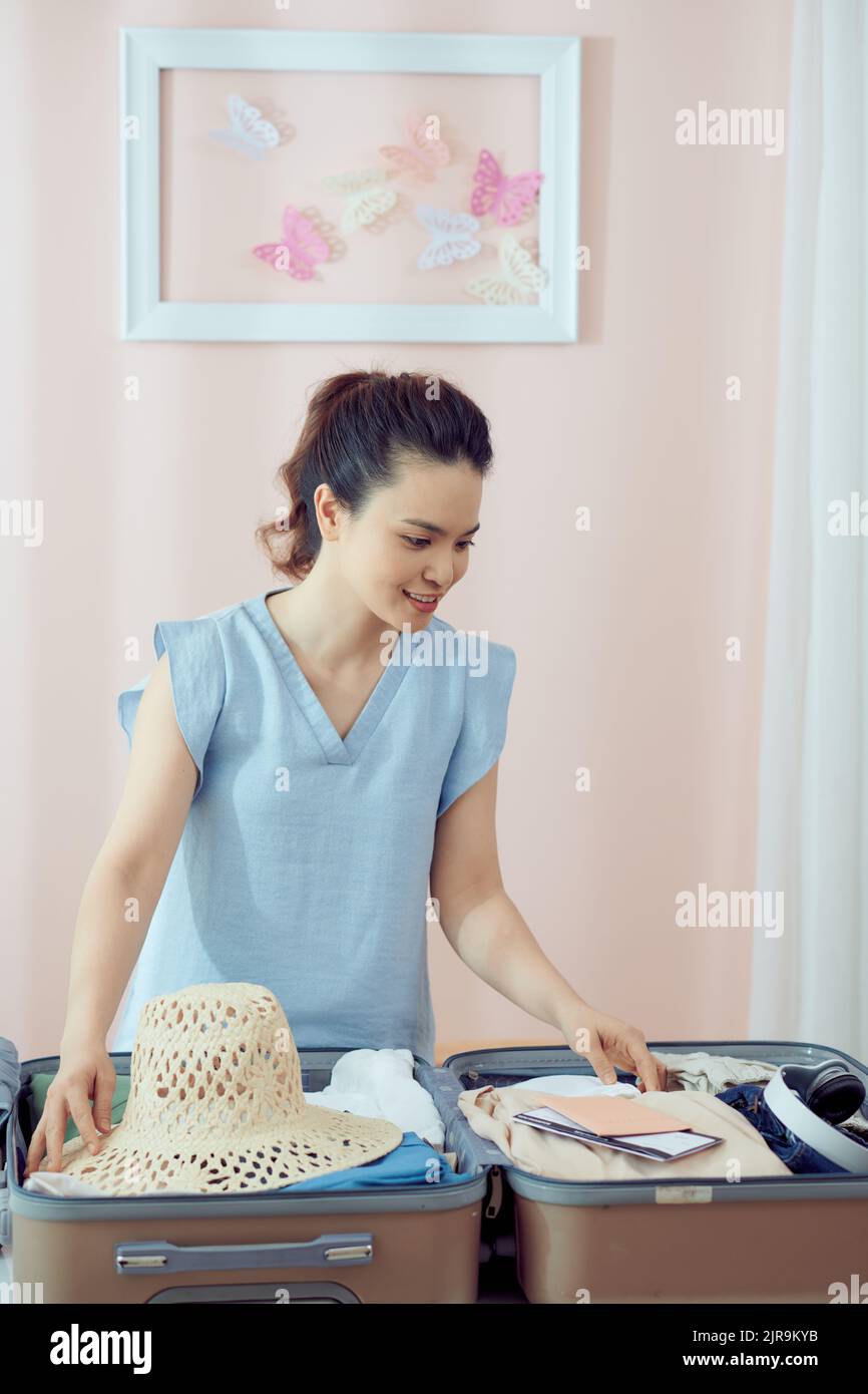 Happy woman is carefully packing colorful summer clothes into luggage ...