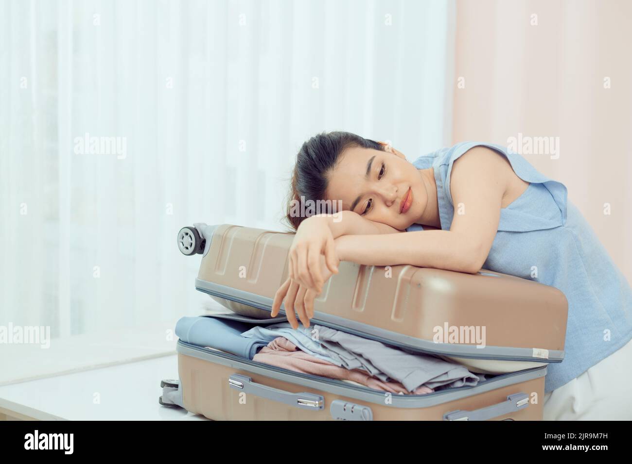Woman standing on her knees on an overfilled suitcase with clothing ...