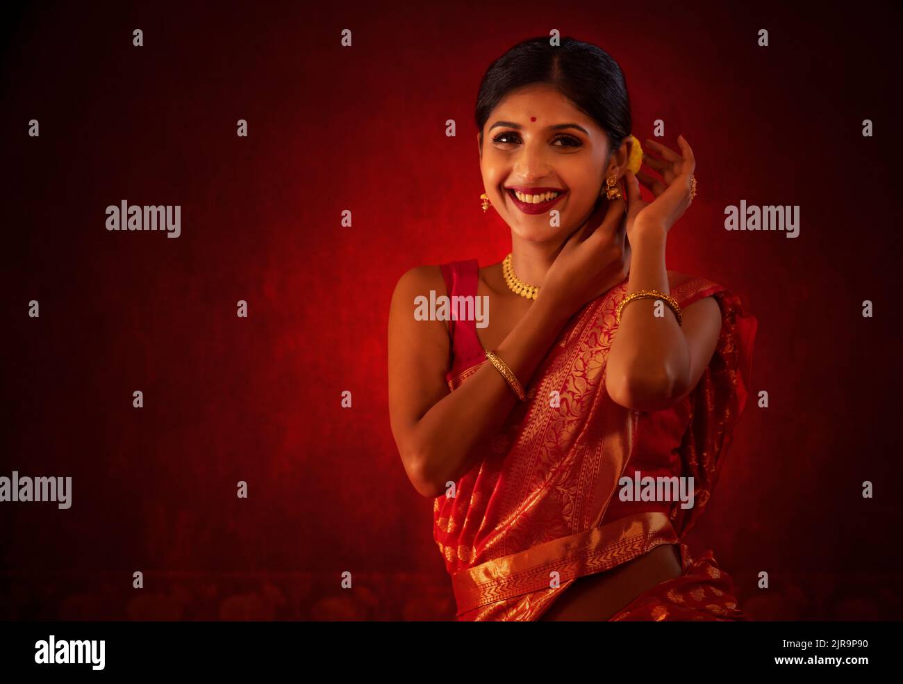 Smiling Indian woman in traditional outfit adjusting flower in her hair ...