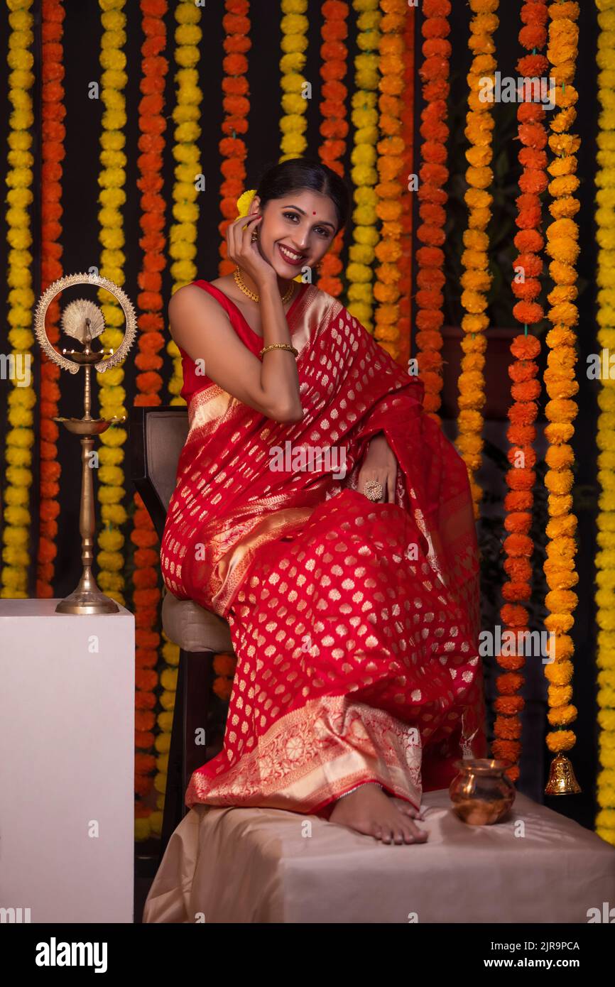 Cheerful woman in red sari sitting on chair against decorated ...