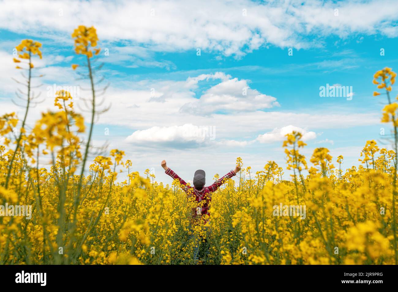 Successful female farmer wearing plaid shirt and trucker hat with arms raised in the air in ...