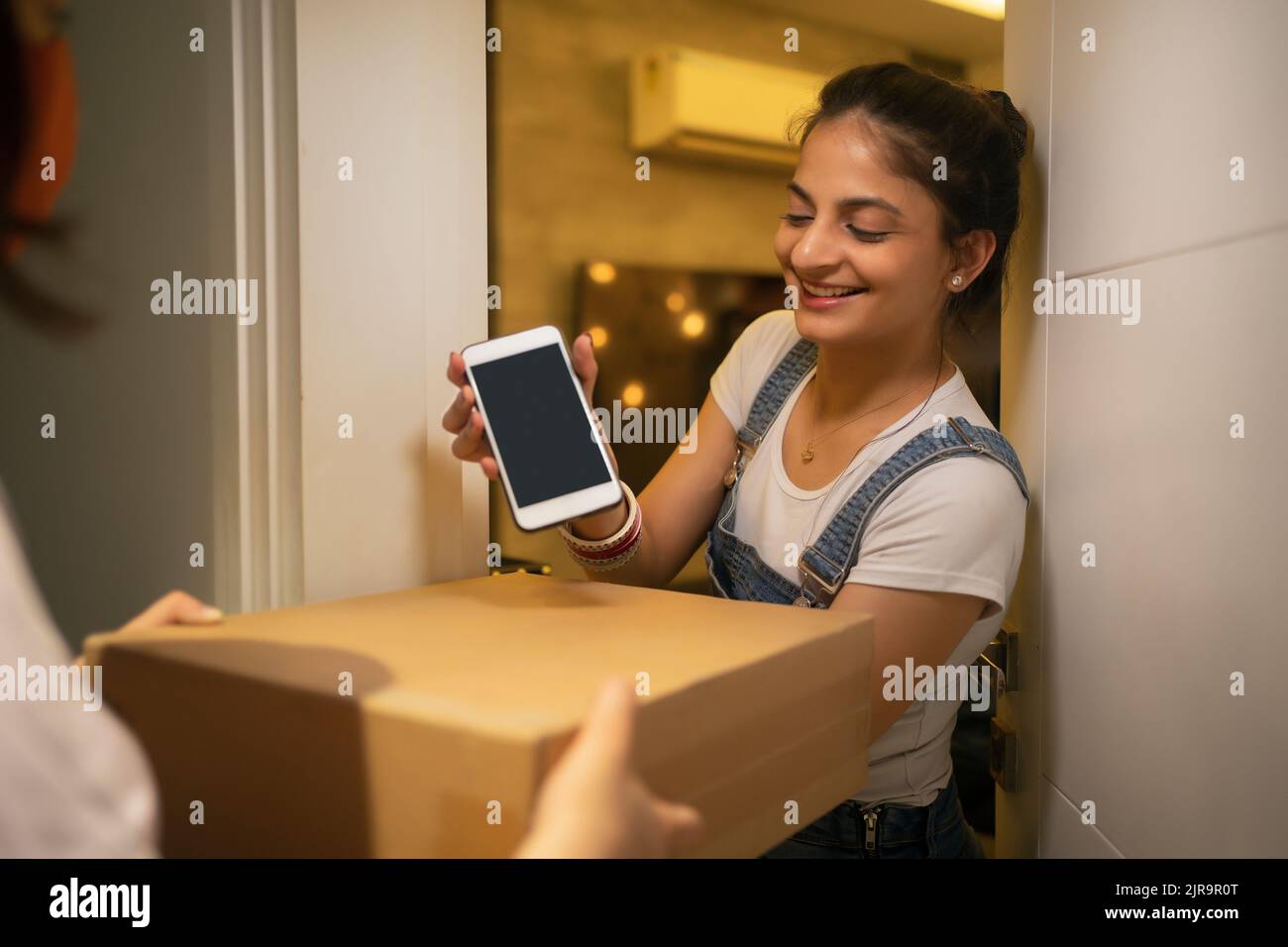 Young woman accepting delivery package at the doorstep with mobile in ...