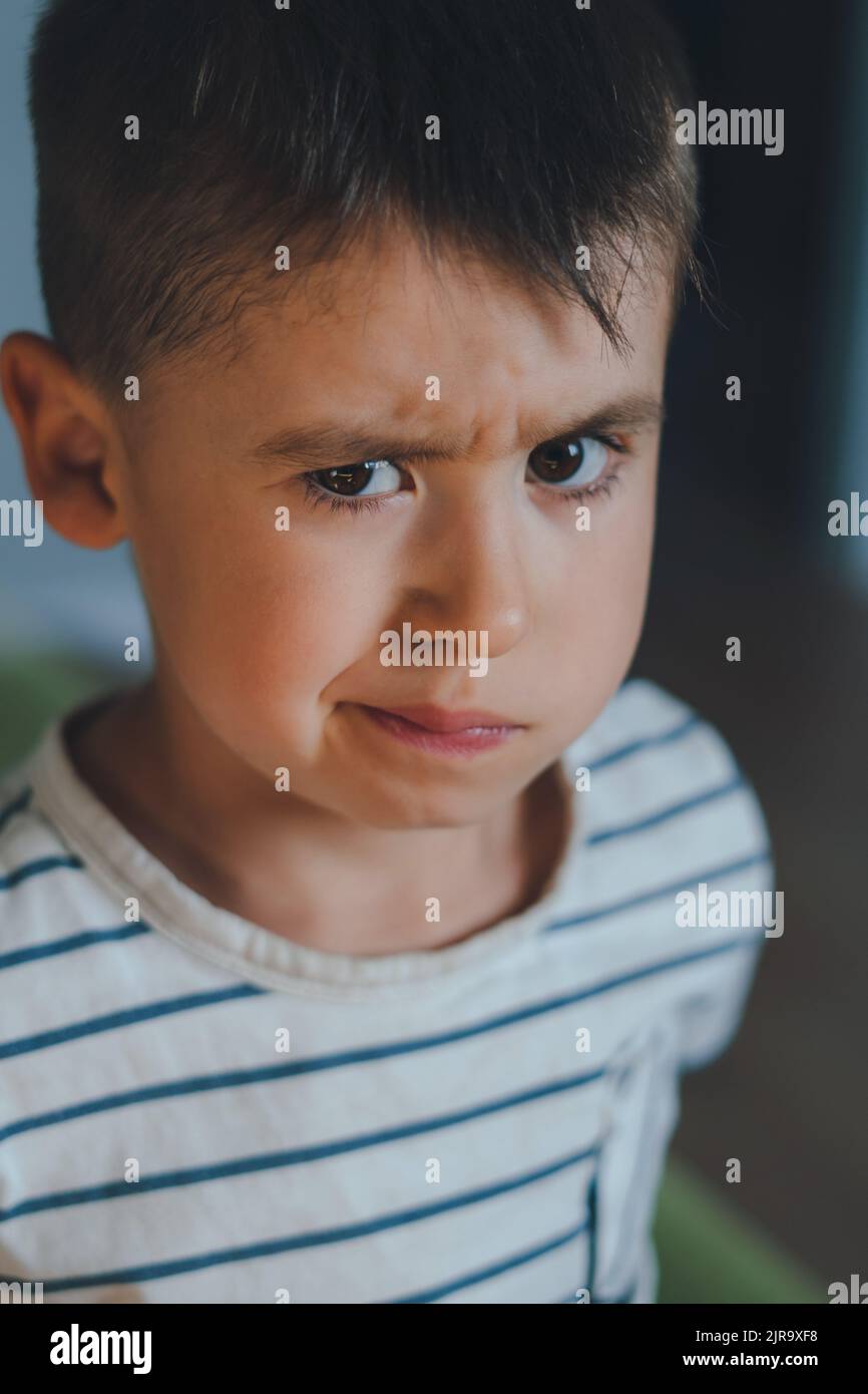 Child grimaces while standing at home, posing looking at camera ...