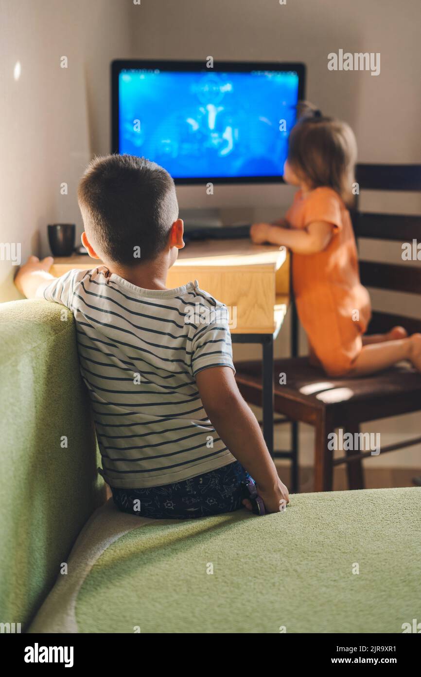 Rear view of a boy sitting on the sofa watching a cartoon on the ...