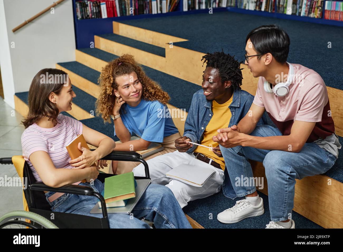 Diverse group of young people discussing work in college library ...