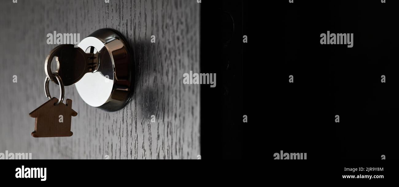 Key with a trinket in the form of a house in the door lock of an open ...