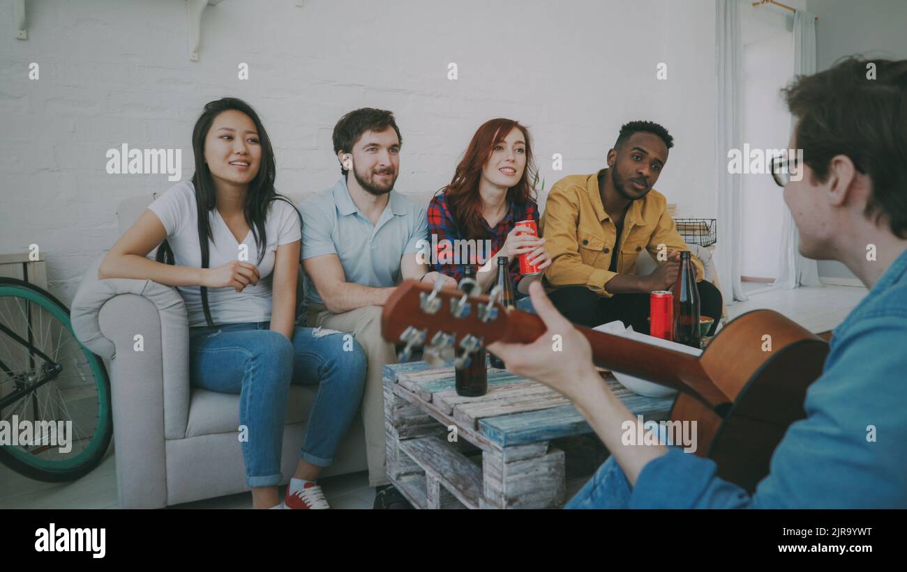 Happy young friends have party at shared apartment and singing together ...