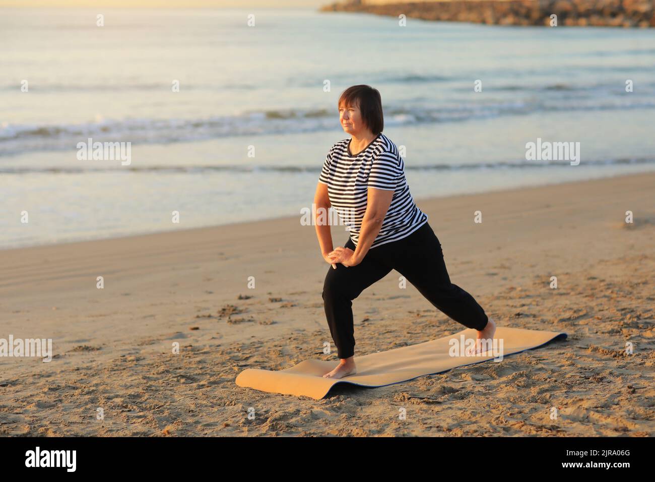 Mature female takes care of body and does yoga by the sea outside on ...