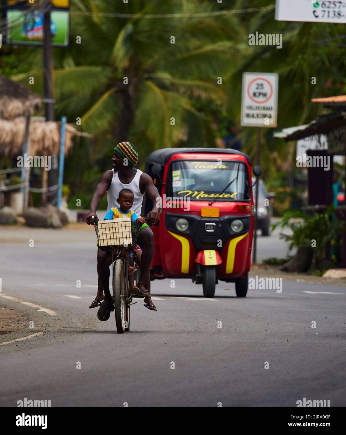 A local man riding a bicycle with his child on a road in the daylight ...