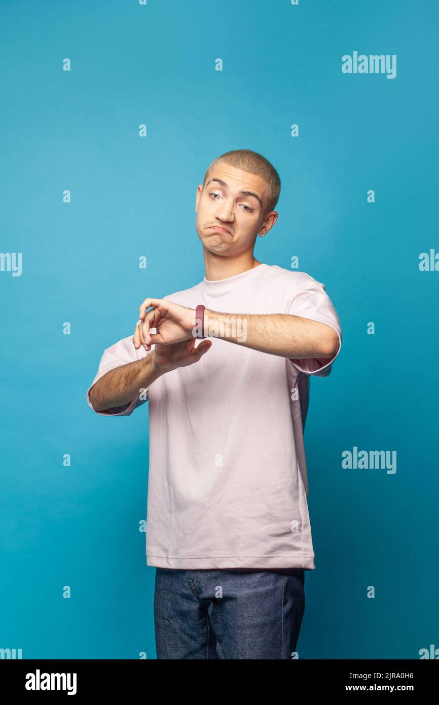 Young man looking at watch on blue background Stock Photo - Alamy