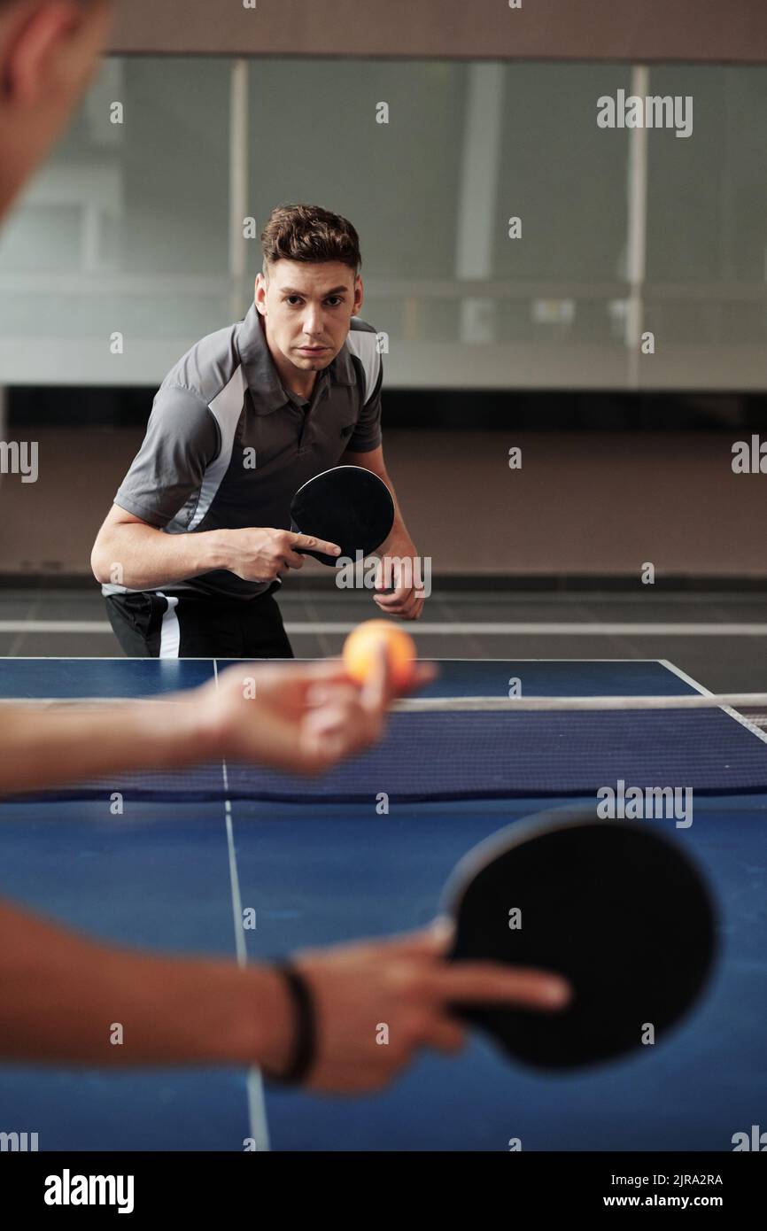 Serious young man playing table tennis with friend in gym when training ...