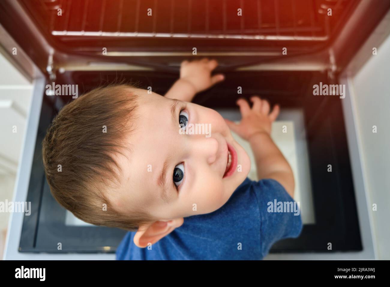 Toddler baby climbs into a hot electric oven. Child boy opens oven door ...