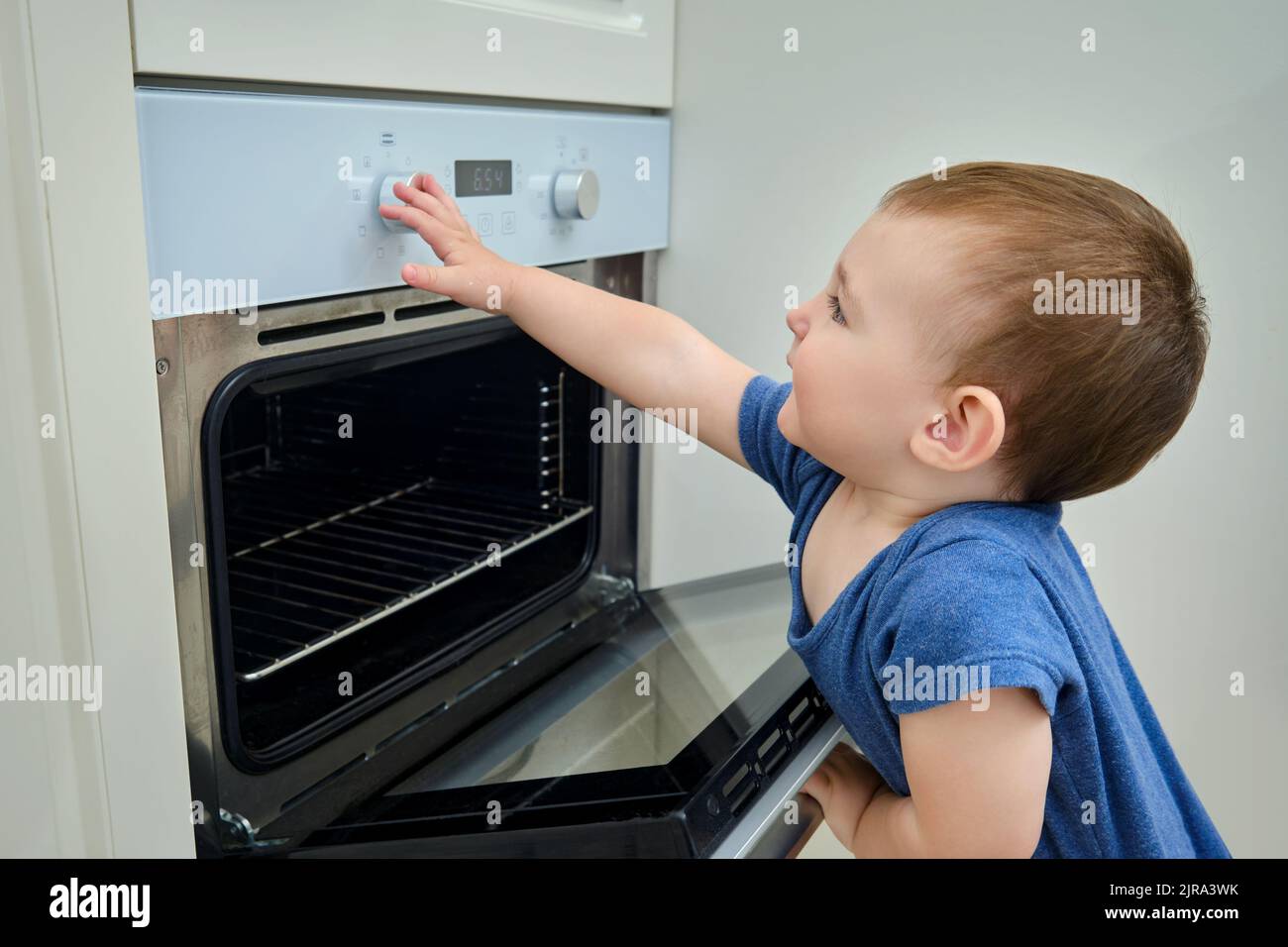 Toddler baby climbs into a hot electric oven. Child boy opens oven door ...
