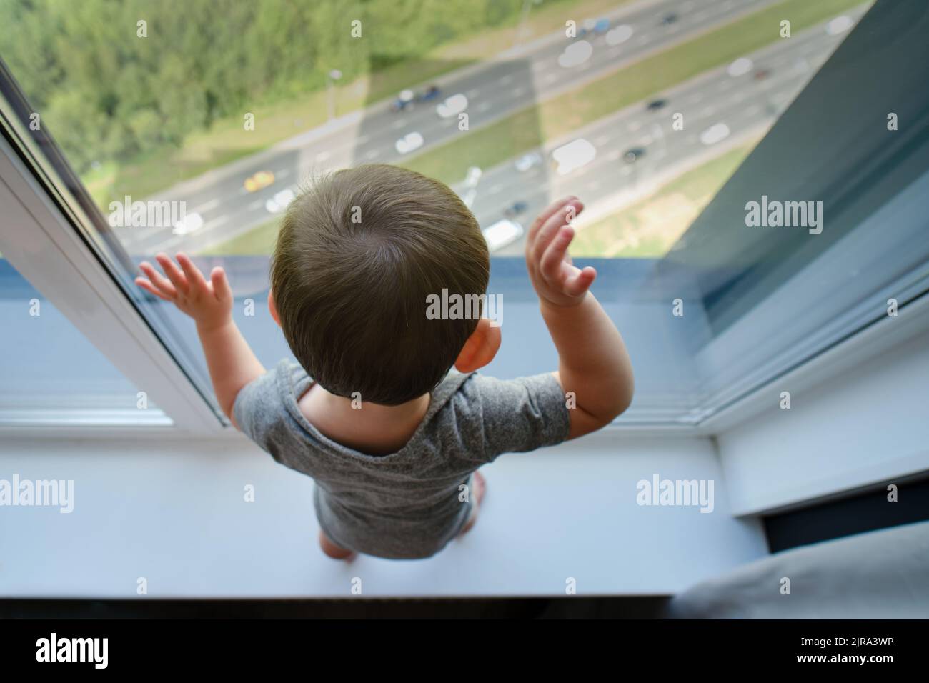 Toddler baby is standing by the window on the windowsill. Child at the ...