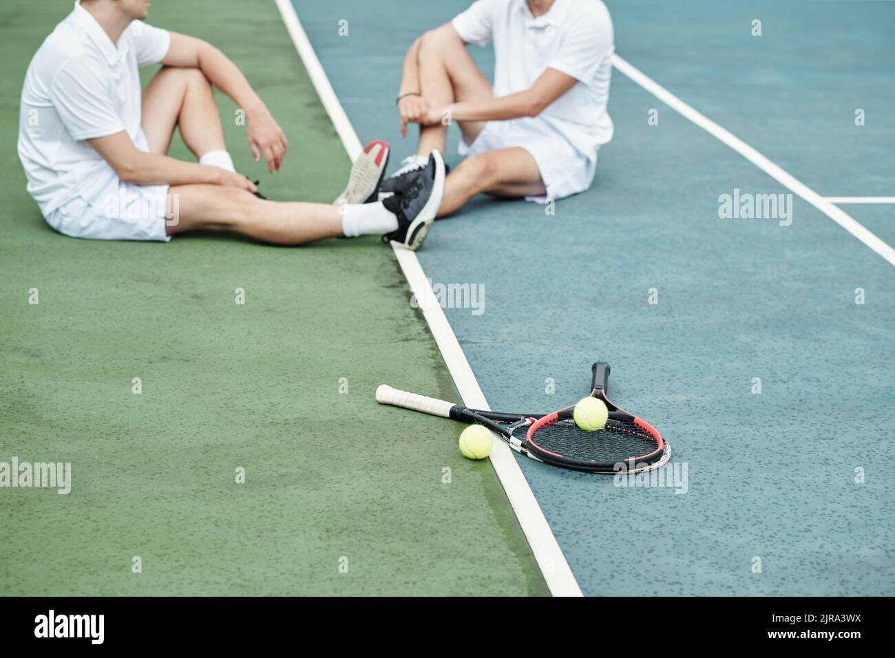 Tennis rackets and balls on court next to sportsmen resting after game ...
