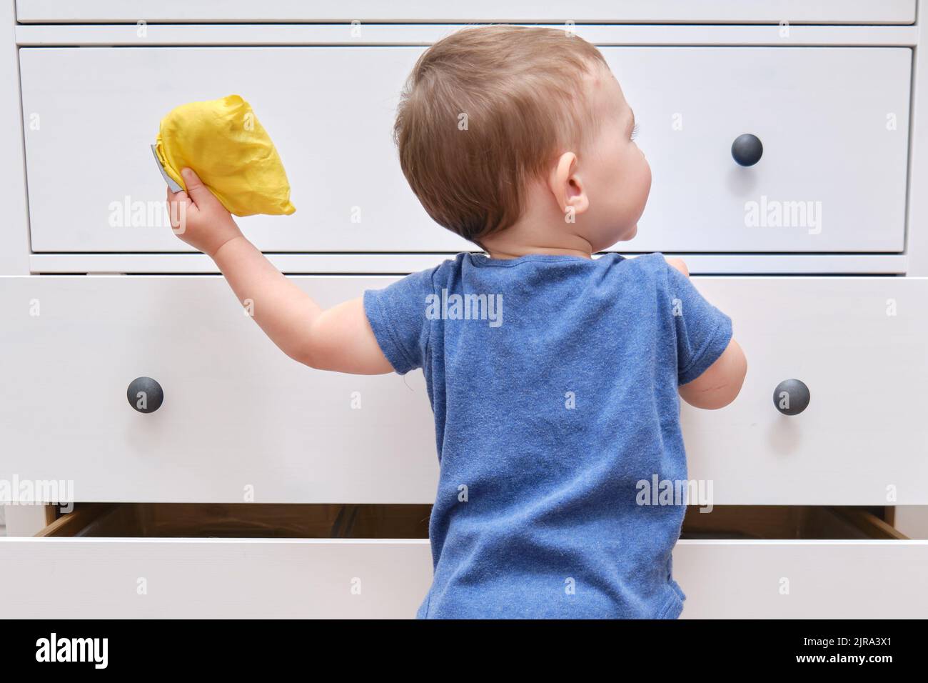 Toddler baby opens a chest of drawers. Child boy reaches into an open ...