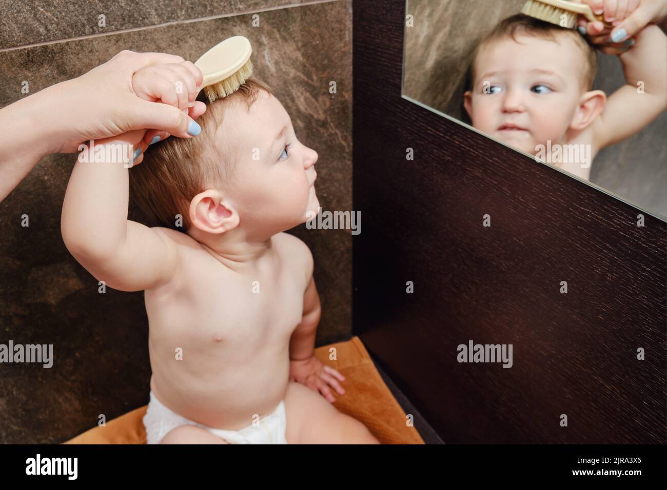Mother teaches to comb the hair to a happy toddler baby boy. Mom makes ...