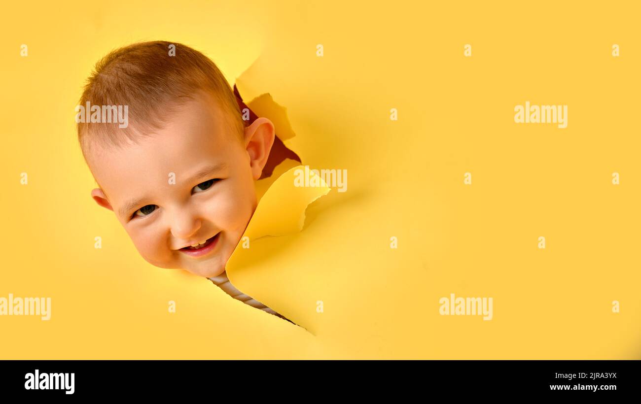 A happy child looks out of a hole in the studio yellow background ...