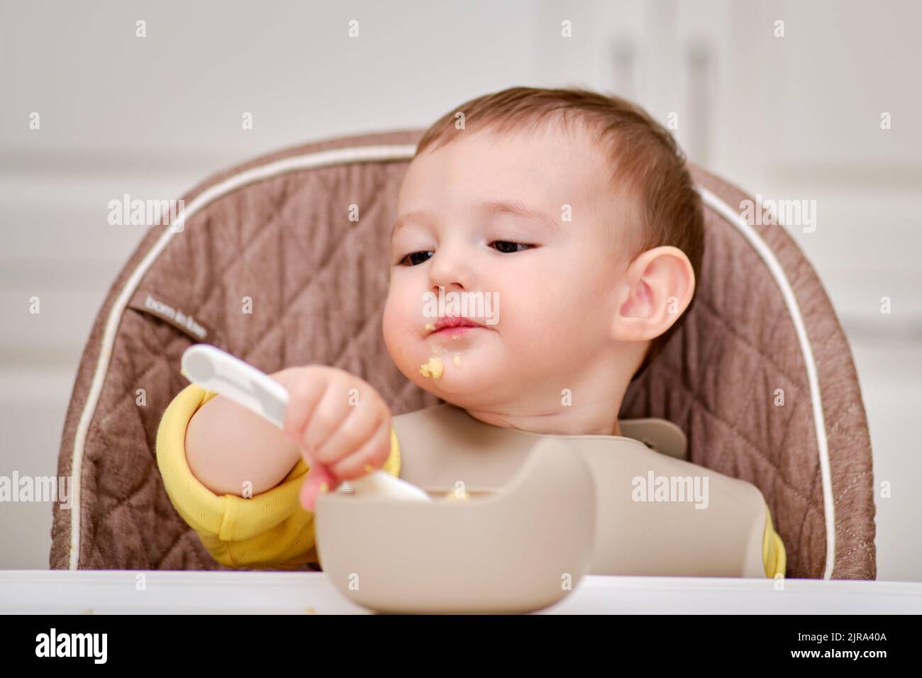 Happy toddler baby boy learns to eat porridge himself with a spoon ...