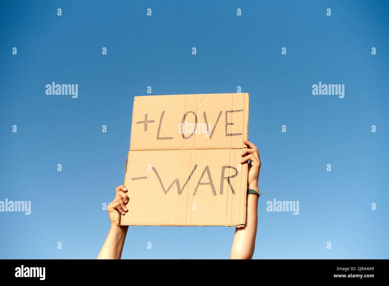 A cardboard sign saying more love and less war held by two hands on ...
