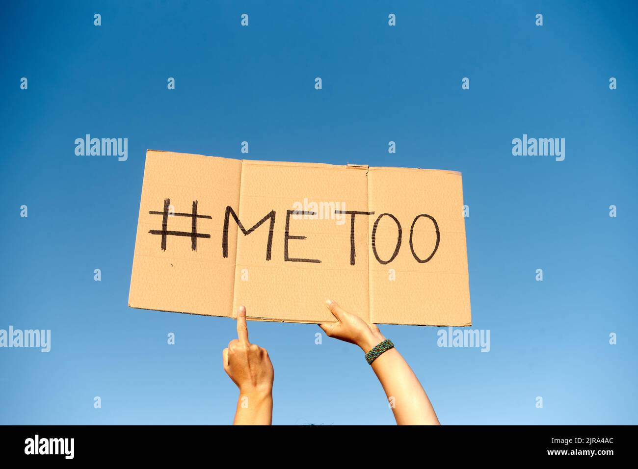 A cardboard sign saying hashtag Me Too held by two hands on clear blue ...