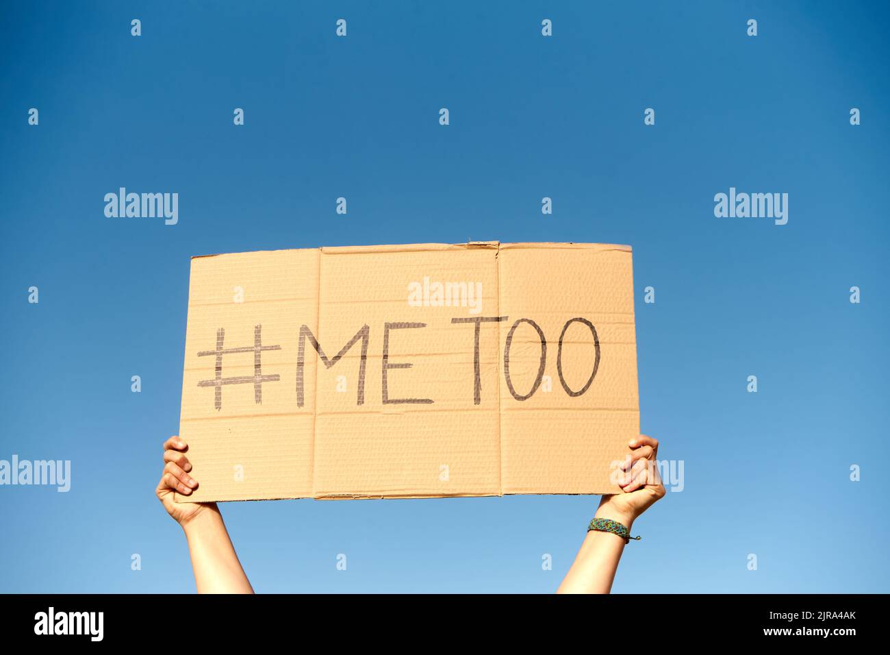 A cardboard sign saying hashtag Me Too held by two hands on clear blue ...