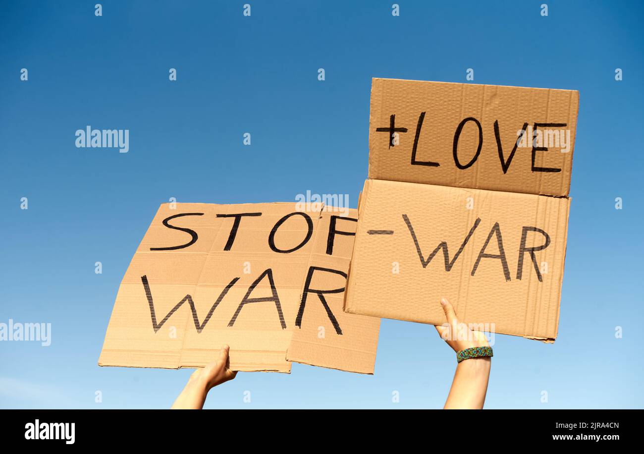 A cardboard sign saying more love, less war, and stop war held by two ...