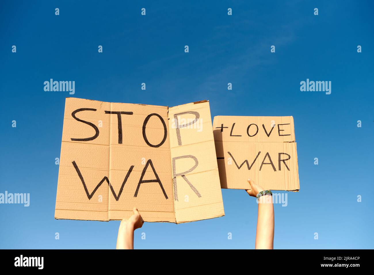 A cardboard sign saying more love, less war, and stop war held by two ...