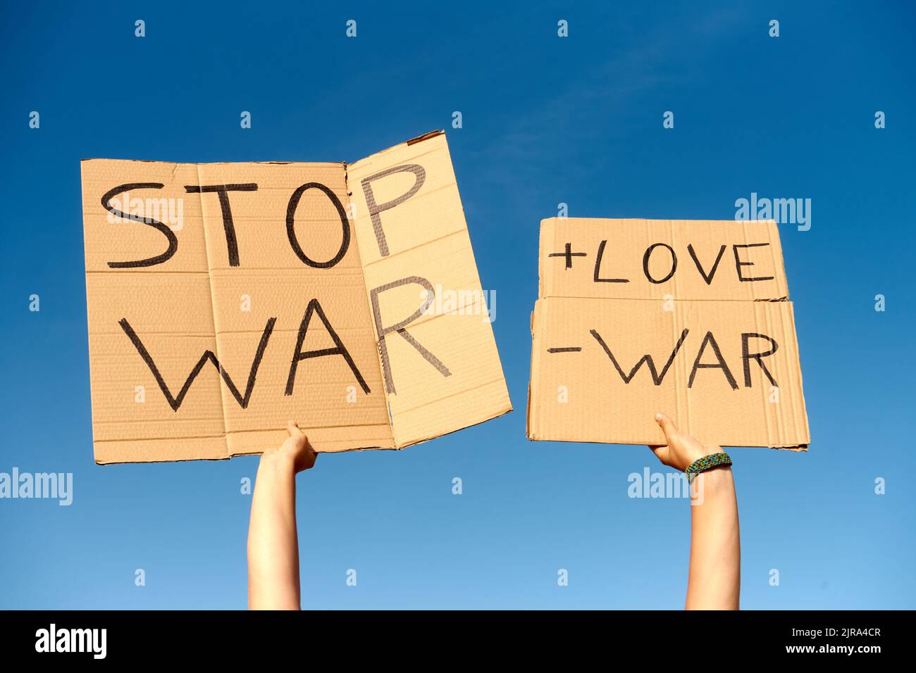 A cardboard sign saying more love, less war, and stop war held by two ...