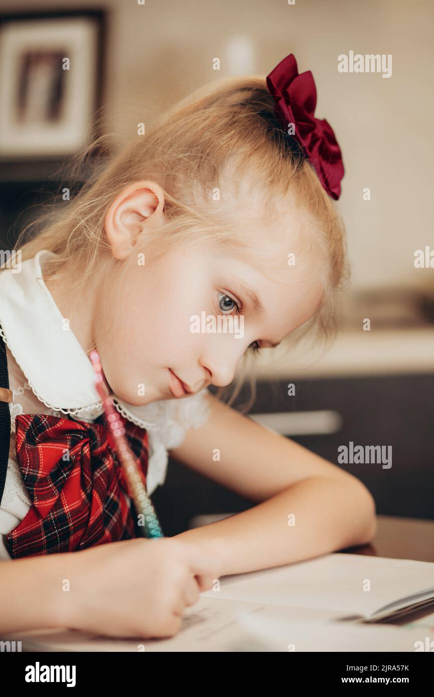 A little girl in a school uniform is doing homework in a exercise book ...