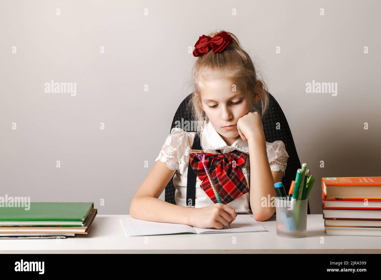 A little girl in a school uniform is doing homework in a exercise book ...
