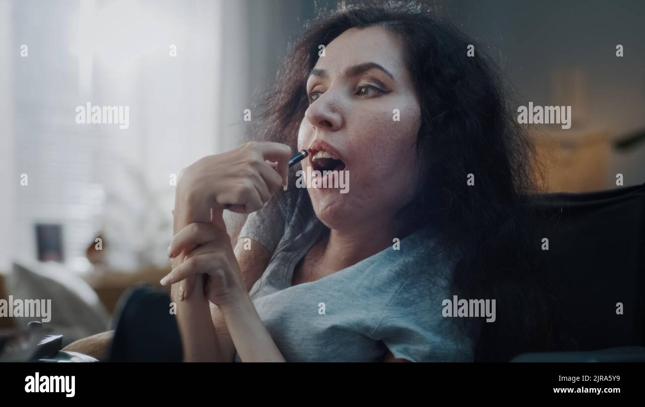 At home woman with disability in a wheelchair doing makeup at the table ...