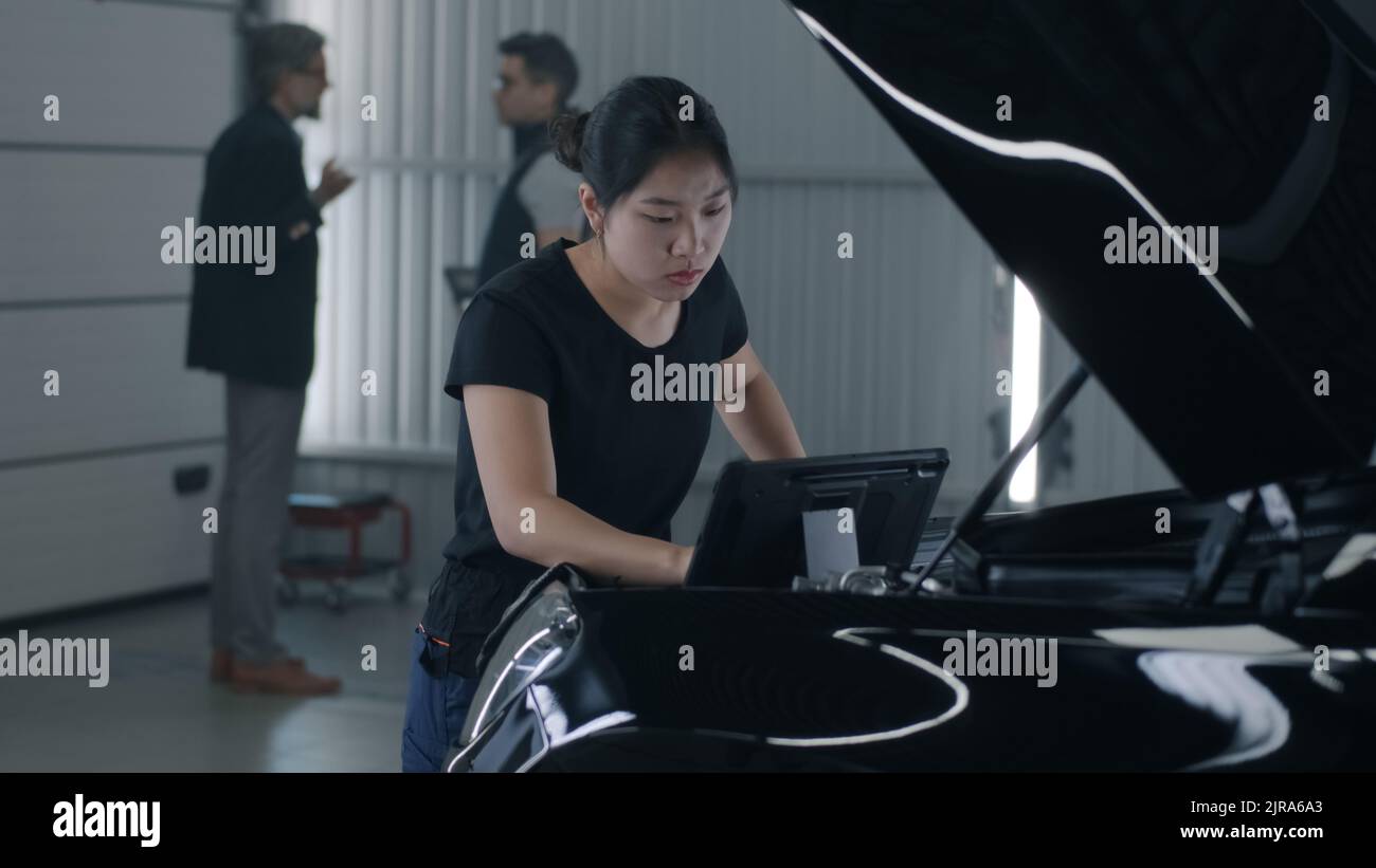 An asian female mechanic in uniform in a car service inspecting and ...