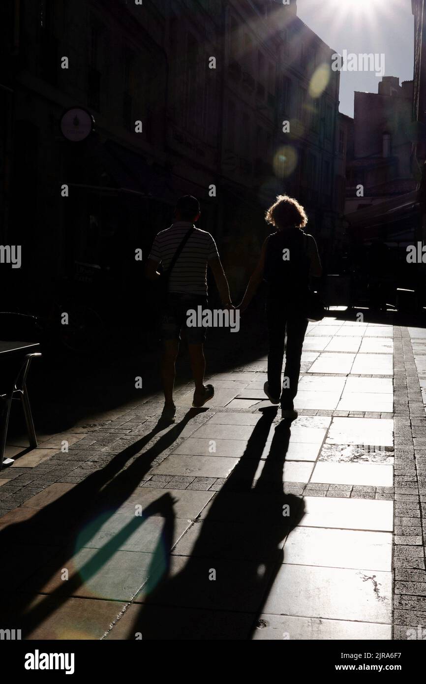 A couple holding hands as they walk in the sun, casting a long shadow ...