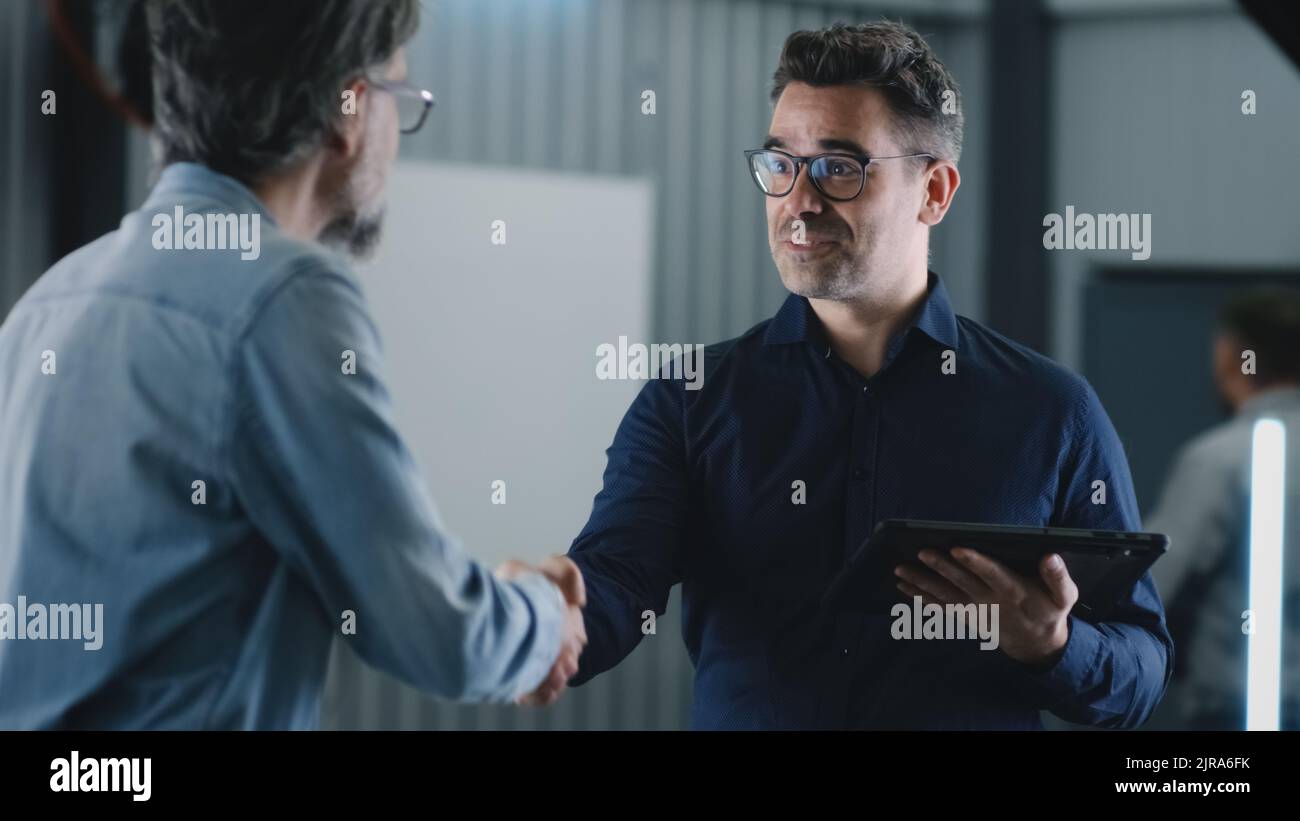 Manager in a suit with a tablet shaking hands with a male client after ...