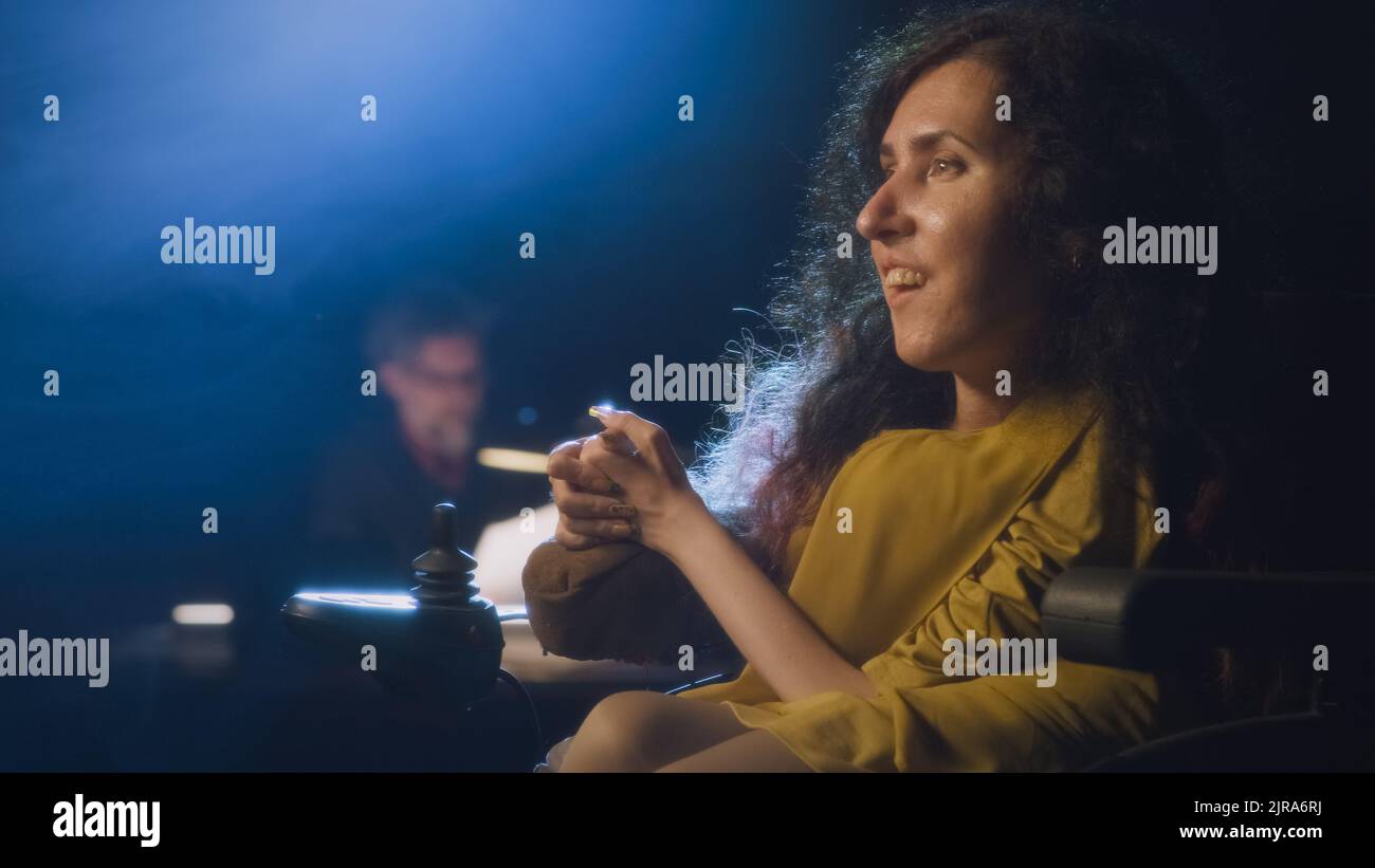 A disabled actress in a wheelchair rehearsing a scene on the dim stage ...