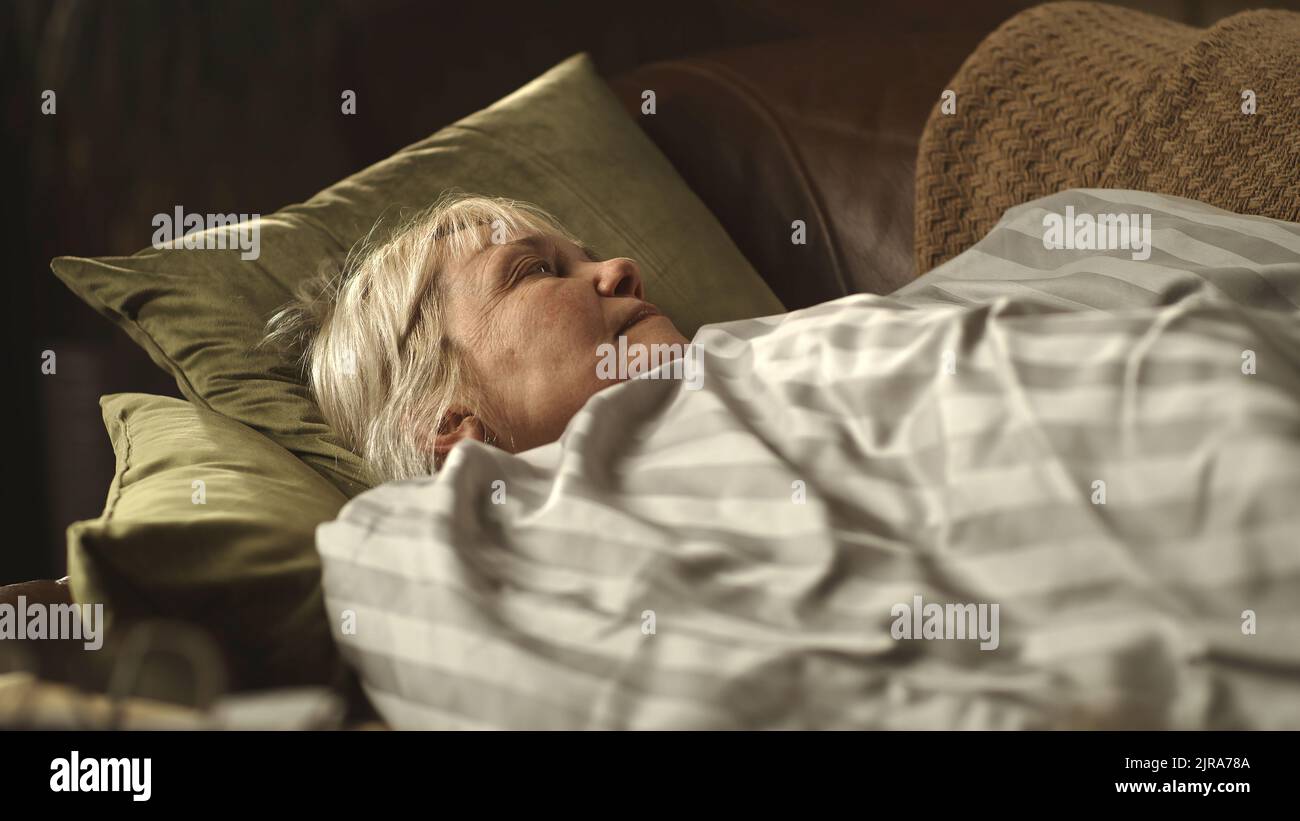 Ill senior female with gray hair tumble uneasy under warm blanket while ...