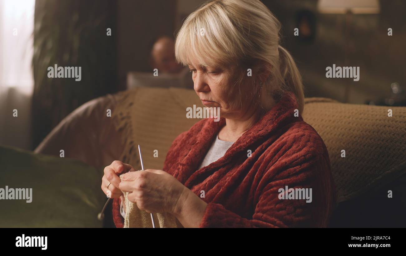 An aged grandmother in a bathrobe creating a warm sweater with knitting ...